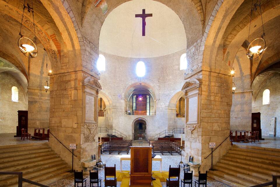 Interior de igreja com arcos de pedra, púlpito de madeira e cruz no teto.