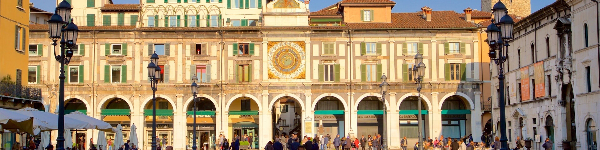 Uma praça histórica com uma torre do relógio imponente, edifícios ricamente decorados e uma área movimentada para pedestres.