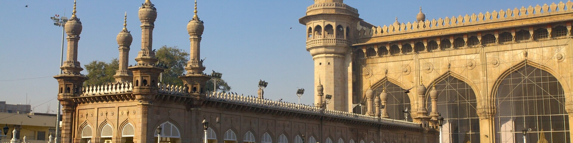 Uma grande mesquita com várias cúpulas e minaretes, rodeada por uma cerca branca e degraus que levam até ela.