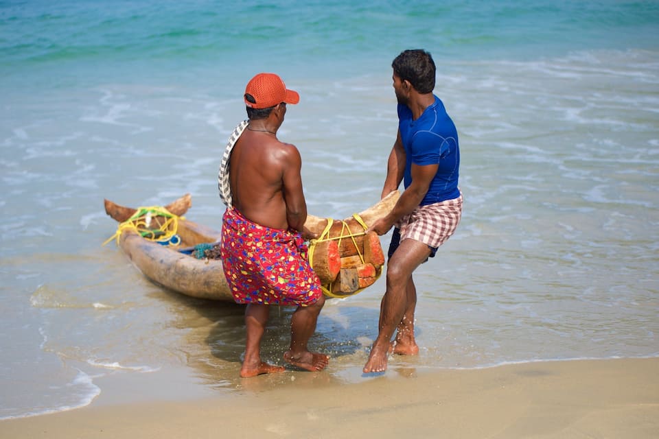 Duas pessoas numa praia com um barco e uma rede.