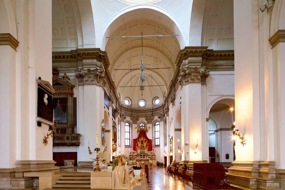 Interior de uma igreja com teto abobadado alto, altar central e fileiras de bancos.