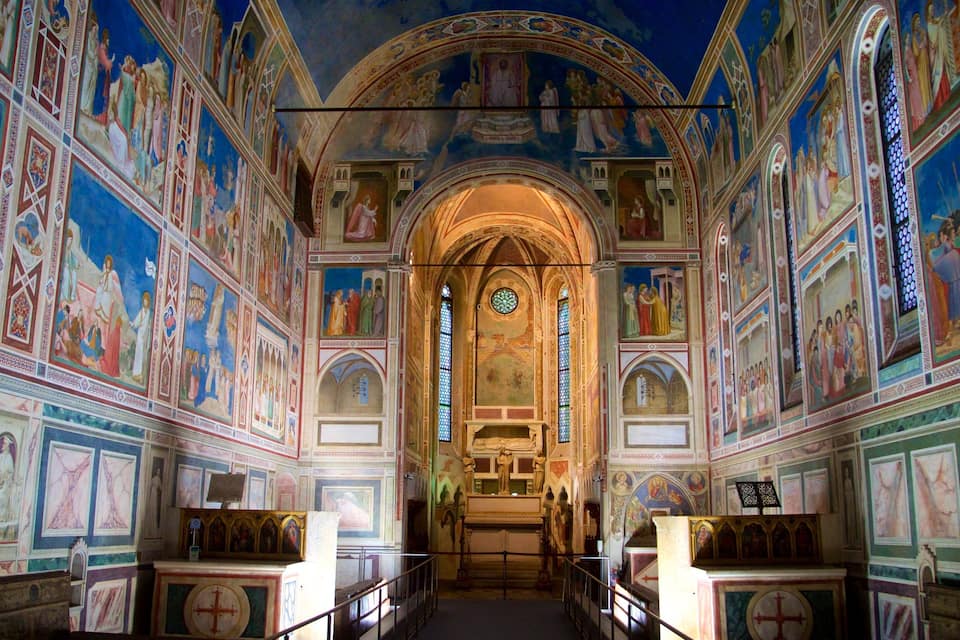 Interior de igreja com afrescos, altar central e vitral.