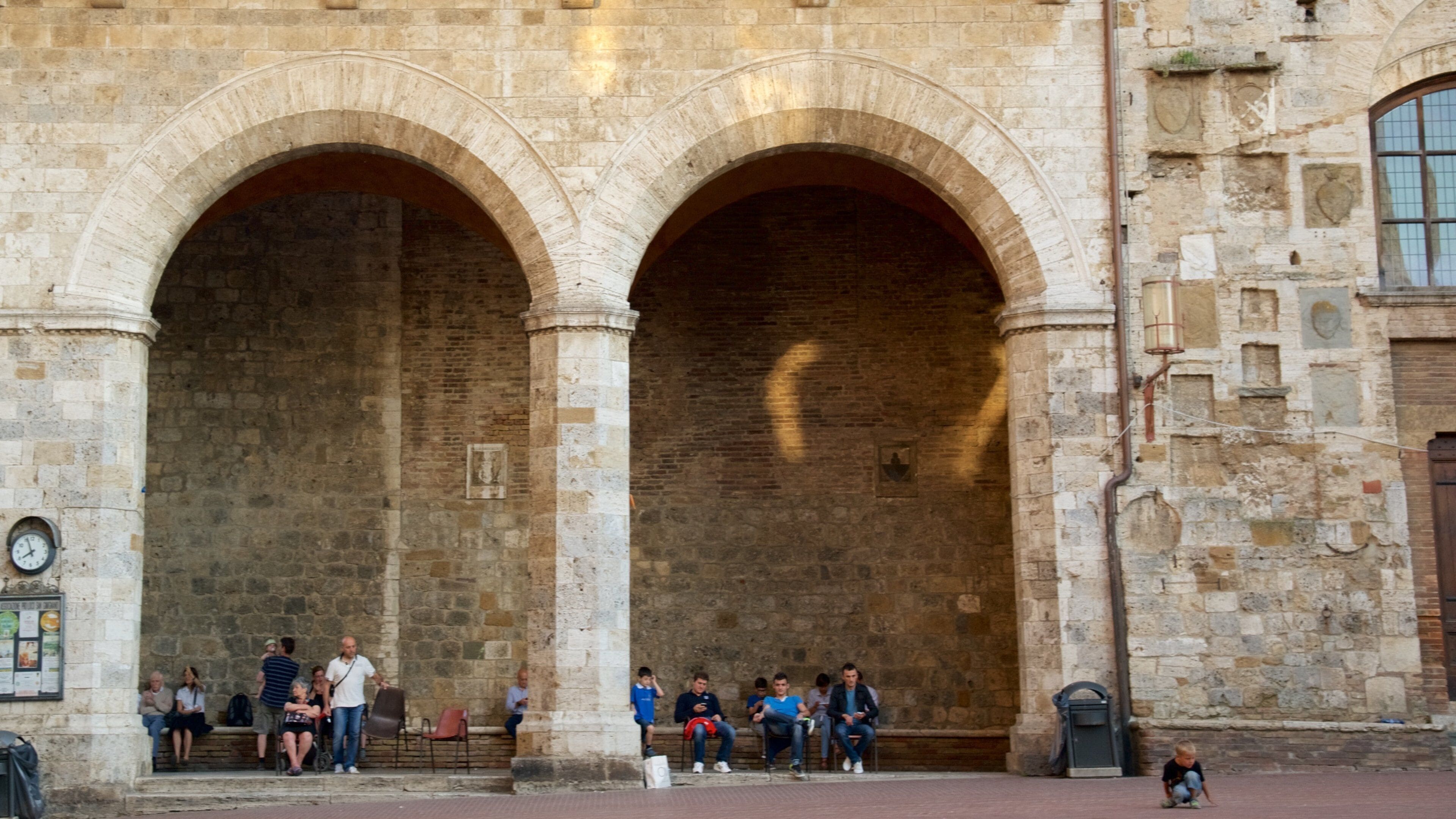 Um arco de pedra com pessoas sentadas e em pé na frente.