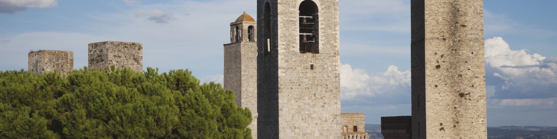 Uma igreja de pedra histórica com duas torres imponentes, rodeada por ruínas antigas e uma floresta densa.
