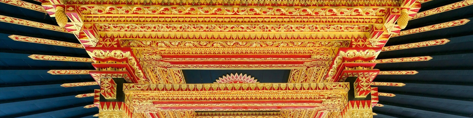 Uma estrutura arquitetônica ornamentada com padrões dourados e vermelhos intrincados, um motivo floral central e um candelabro.