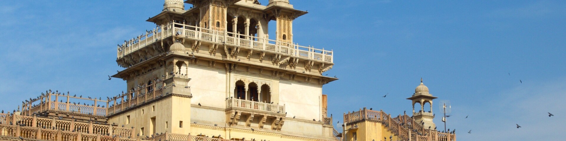 Um edifício histórico com arquitetura ornamentada, incluindo cúpulas e varandas, sob um céu azul límpido.