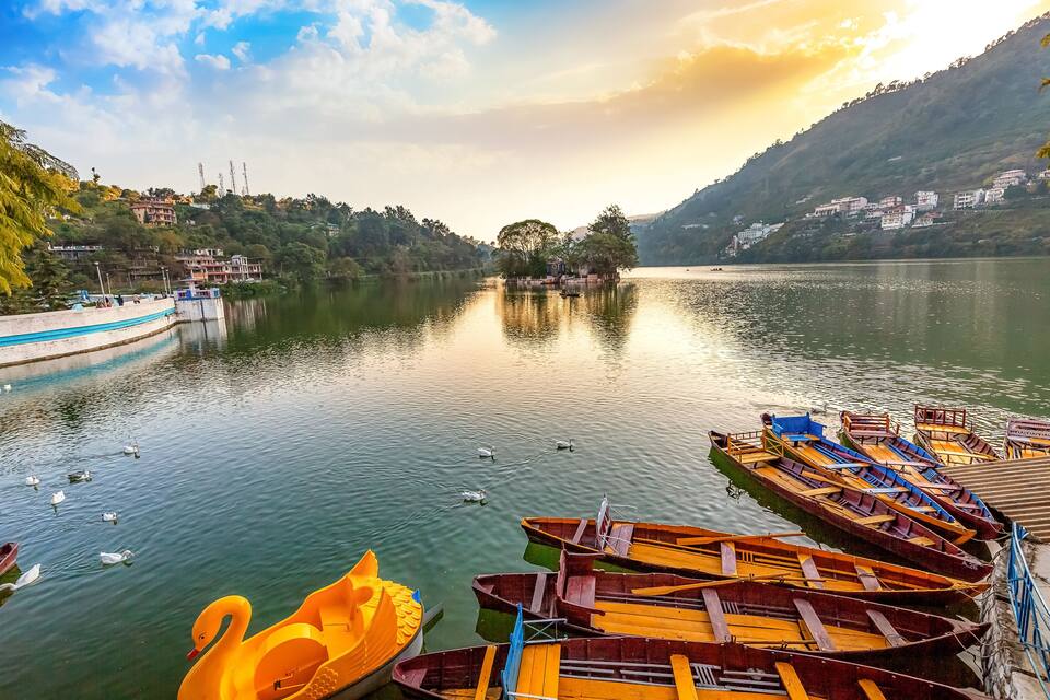 Um lago tranquilo com barcos atracados à direita, cisnes nadando e edifícios nas colinas ao fundo.