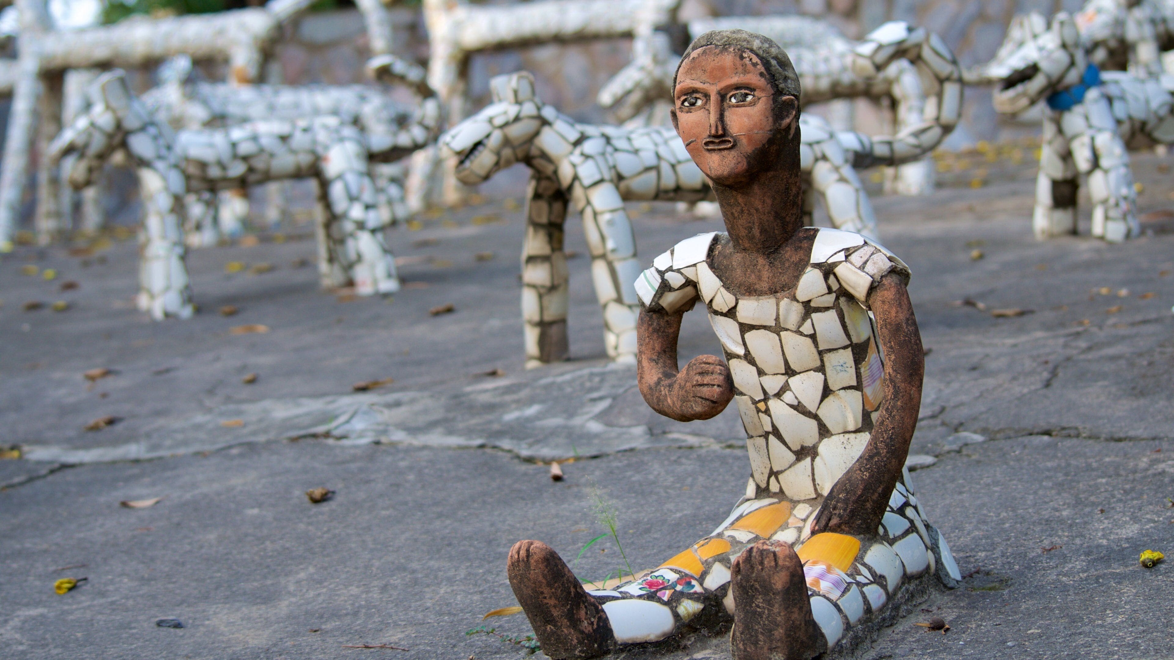 Uma escultura em mosaico de uma figura sentada no chão, rodeada por figuras semelhantes.