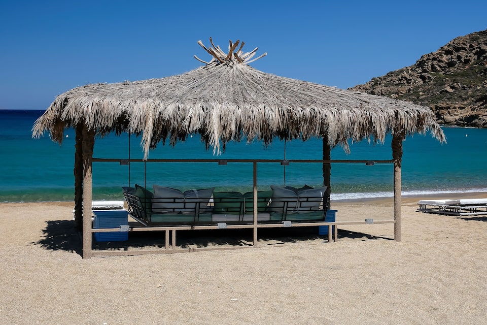 Uma praia com um gazebo de palha, areia dourada e mar azul transparente.