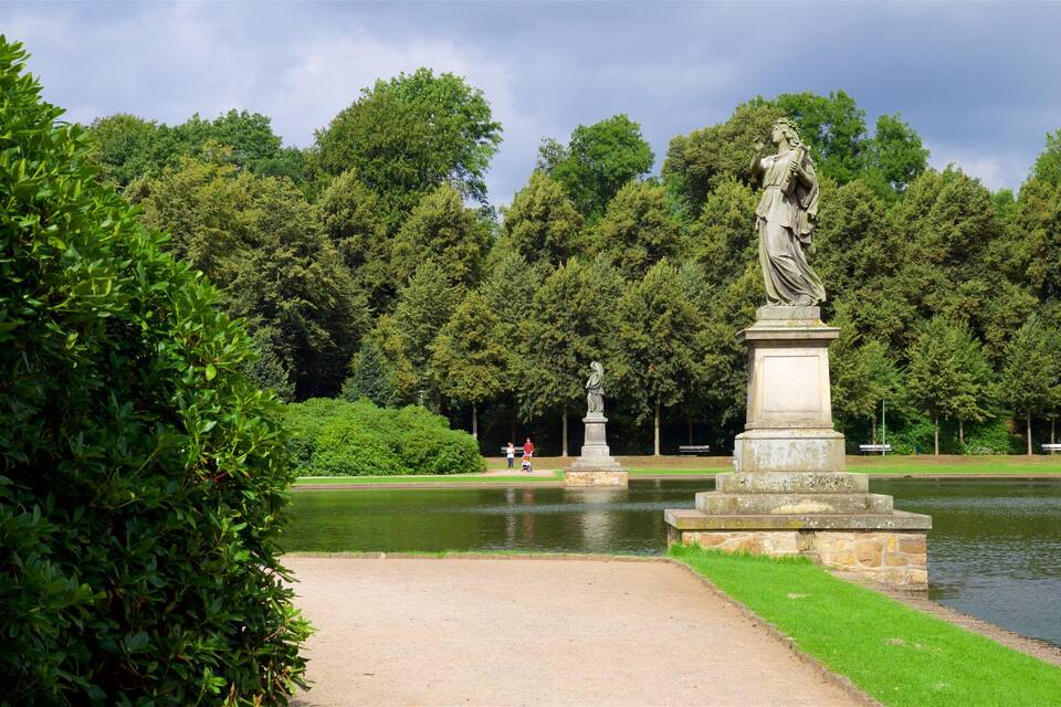 Um parque com uma estátua, um lago e árvores densas.