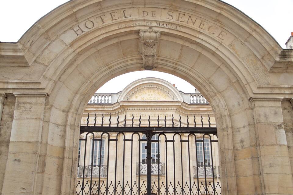 A entrada do Hotel de Sennece, com um arco de pedra ornamentado e um portão de ferro forjado.