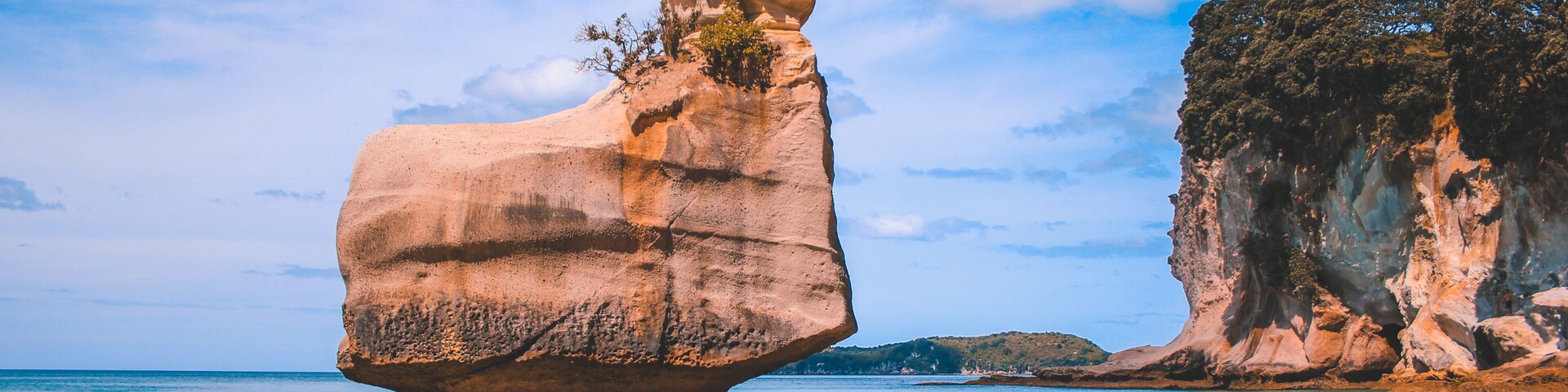 Uma grande formação rochosa numa praia, com céus azuis e límpidos.