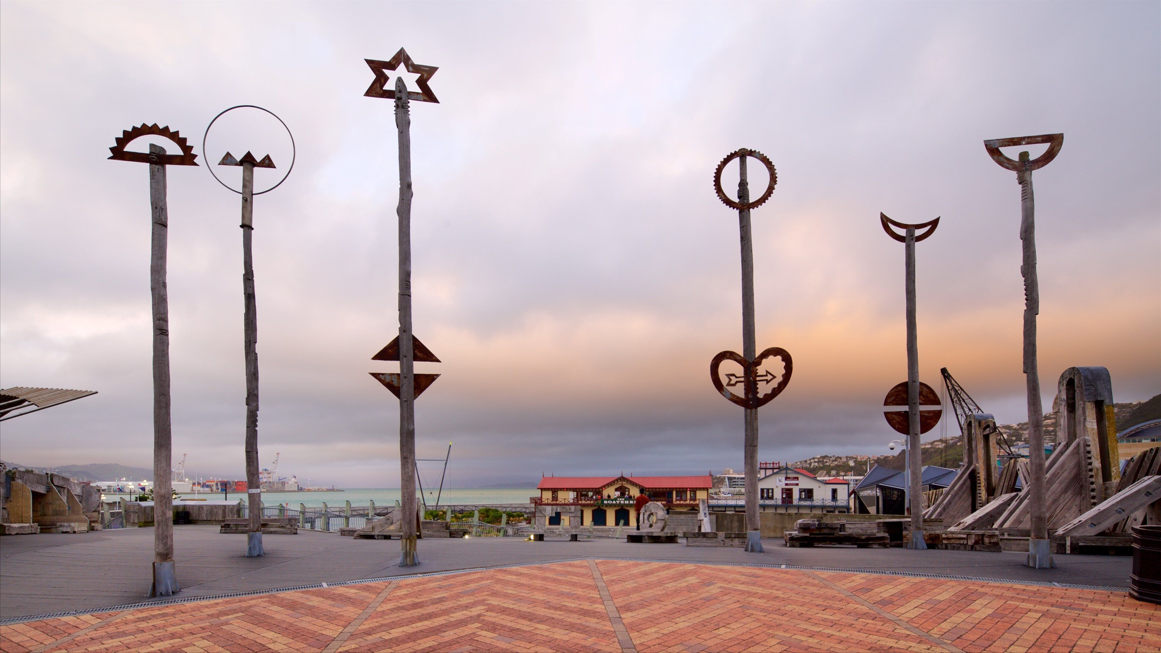 Um calçadão à beira-mar com postes de iluminação urbana artísticos e uma cidade costeira ao fundo.
