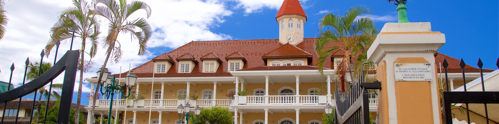 Um edifício grande e amarelo com telhado vermelho e uma torre do relógio.