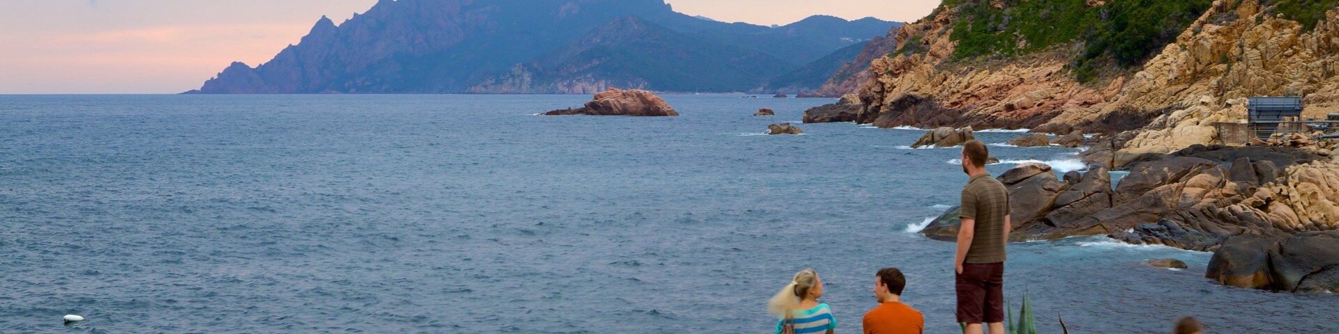 Uma paisagem costeira com um penhasco rochoso, um muro de pedra e um mar calmo.