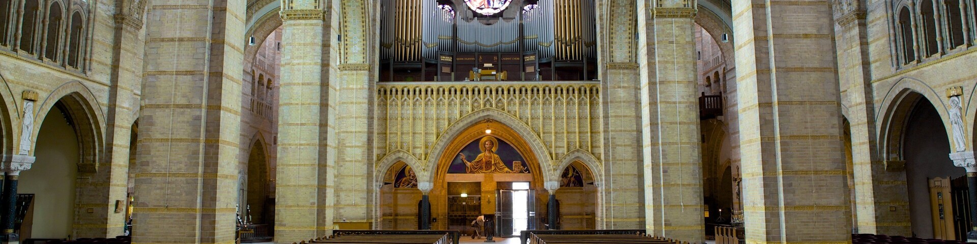 Interior de uma catedral com altos tetos abobadados, fileiras de bancos e janelas de vitrais.