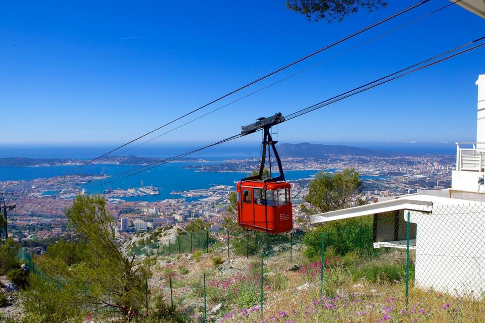 Um teleférico vermelho sobre uma cidade costeira com céu azul límpido.