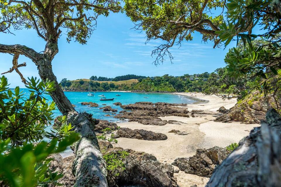 Paisagem costeira com praia arenosa, afloramentos rochosos e barcos na água.