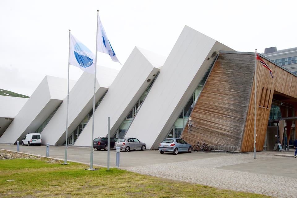 Um edifício moderno com um design angular único, fachada de madeira e várias bandeiras.