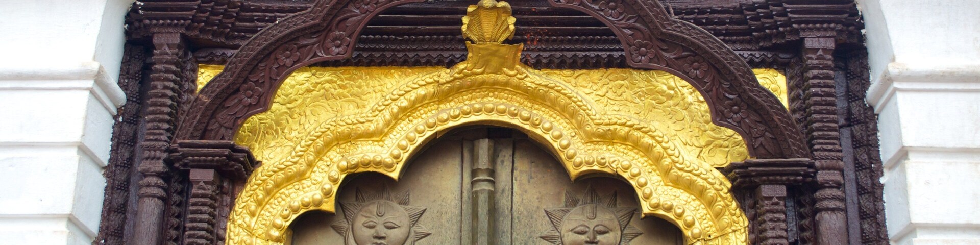Uma entrada arquitetônica detalhada com esculturas ornamentais e arco dourado.