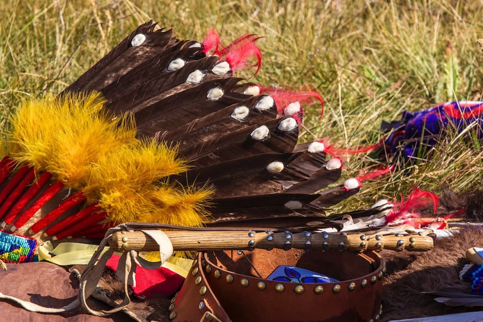 Uma coleção de artefatos tradicionais nativo-americanos, incluindo cocares emplumados, um cinto decorado e uma pequena bolsa com contas.