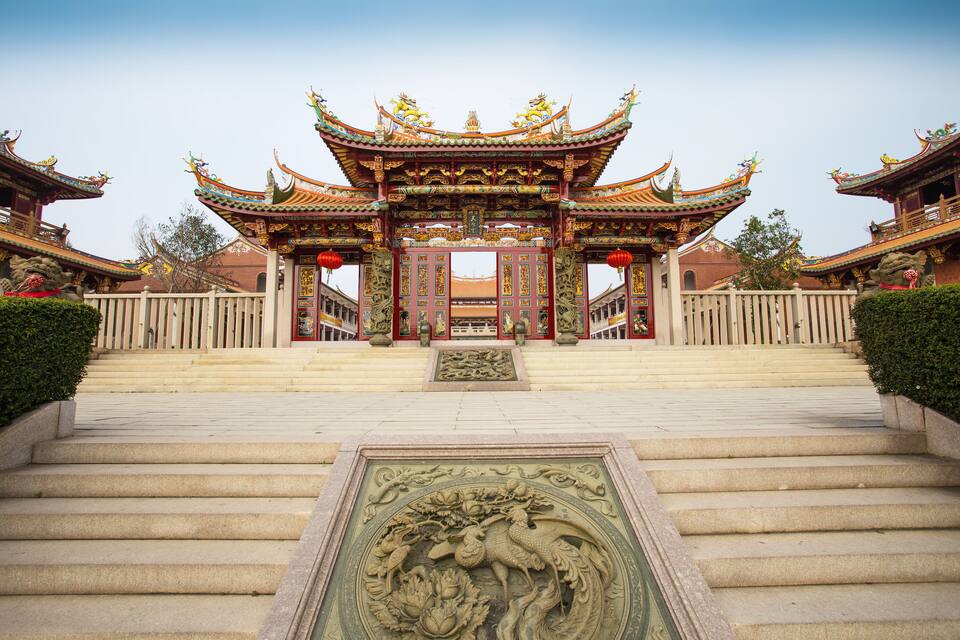 Um portão tradicional chinês com decoração elaborada e uma estátua de leão de pedra na base.