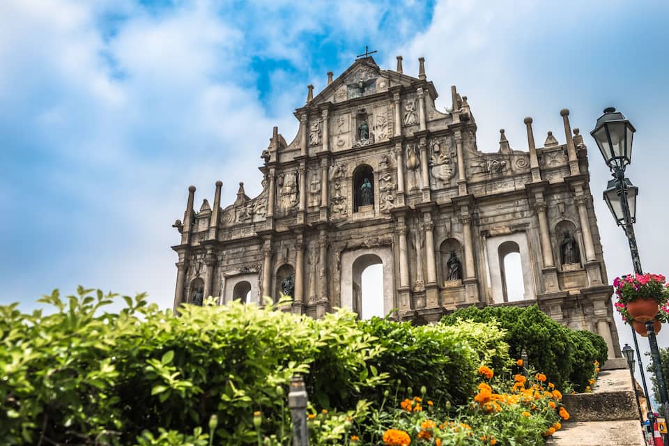 Uma catedral histórica com arquitetura elaborada, céu claro e um lampião com flores.