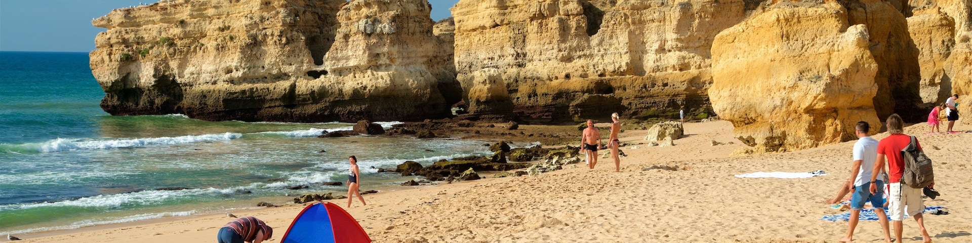 Uma praia arenosa com falésias rochosas e céu azul límpido.