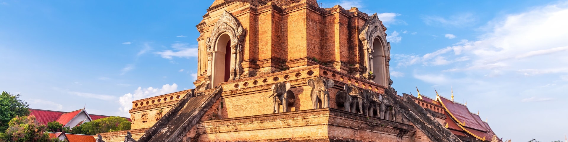 Um templo de tijolos imponente com uma escadaria íngreme, rodeado por plantas em vasos e um céu azul límpido.