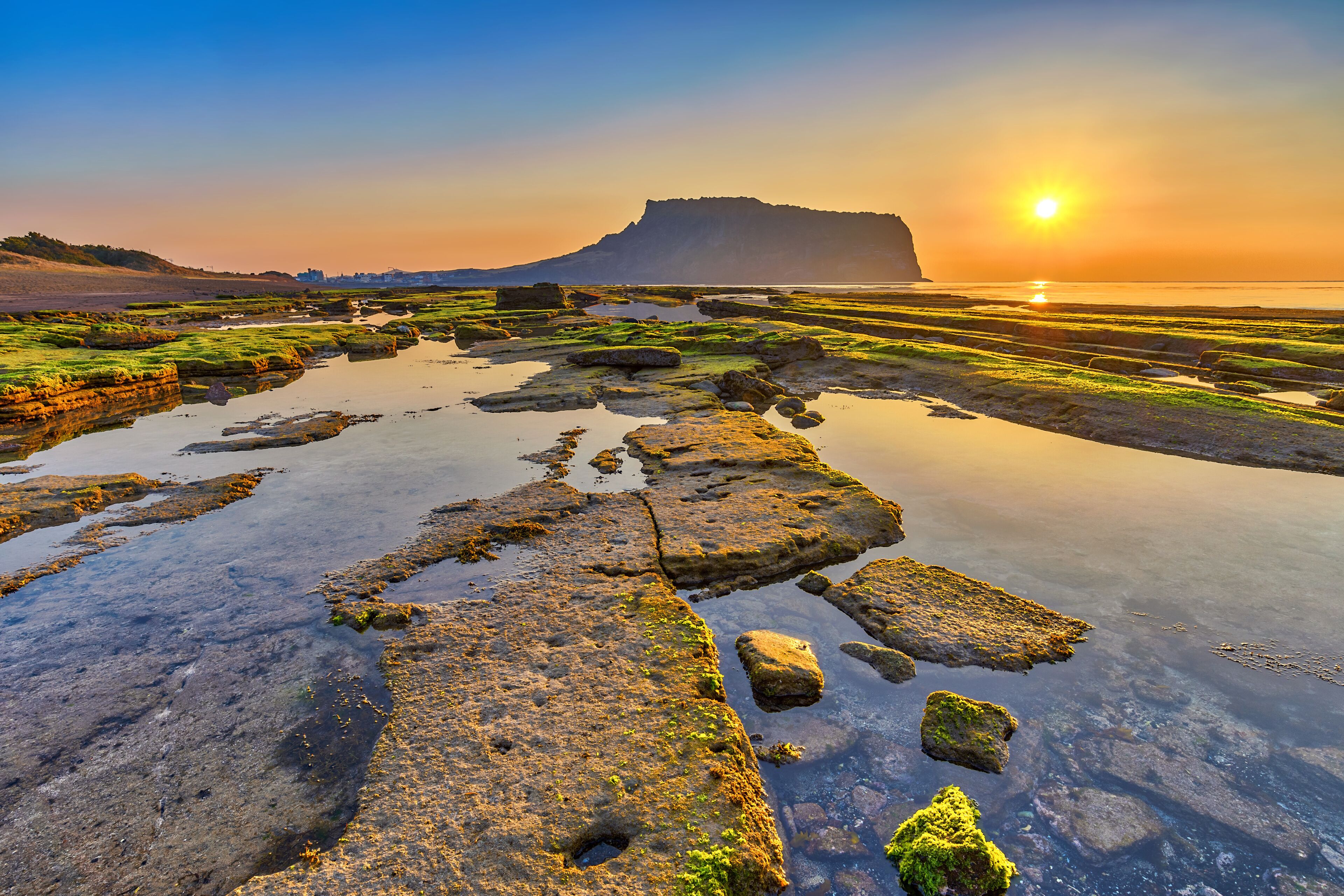 Paisagem costeira com uma formação rochosa imponente e um pôr do sol.