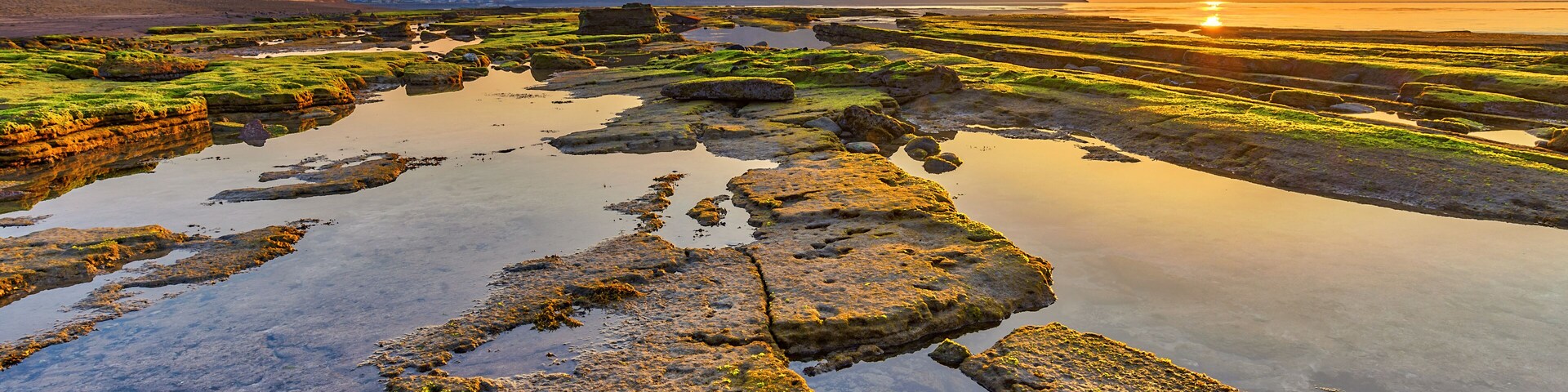 Paisagem costeira com uma formação rochosa imponente e um pôr do sol.