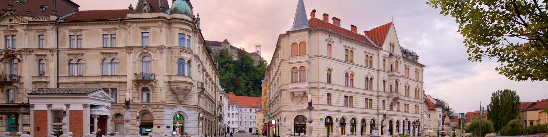 Uma rua de calçada adornada por edifícios históricos, uma ponte com balaústres ornamentados e um castelo distante no topo de uma colina.