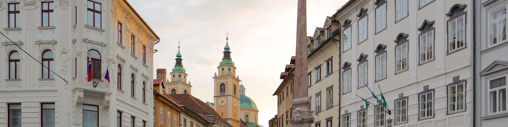 Uma praça histórica com edifícios ornamentados, uma fonte e uma igreja com cúpula verde.