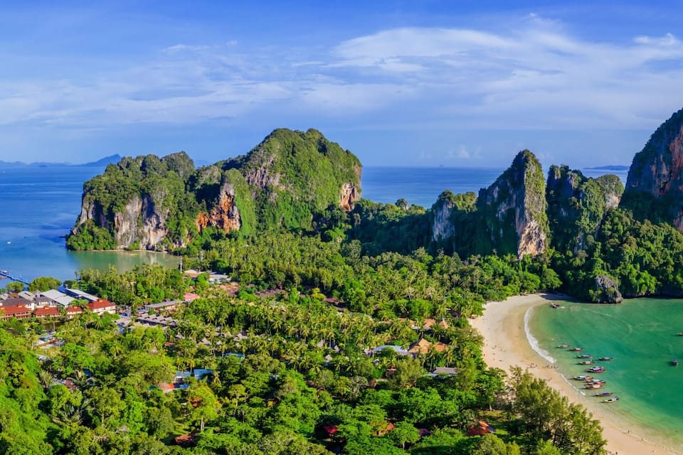 Paisagem costeira com imponentes falésias de calcário, uma praia e um pequeno povoado com casas tradicionais.