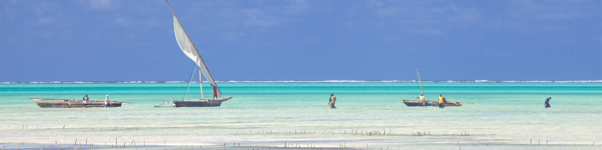 Uma praia com águas turquesa cristalinas, vários barcos pequenos e uma faixa de areia com vegetação rala.