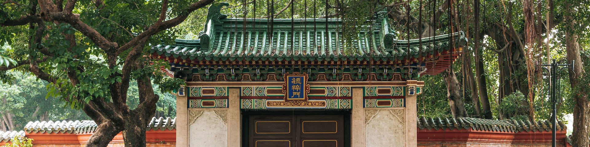 Um portão chinês tradicional com decorações elaboradas e telhado em telhas, rodeado por árvores.