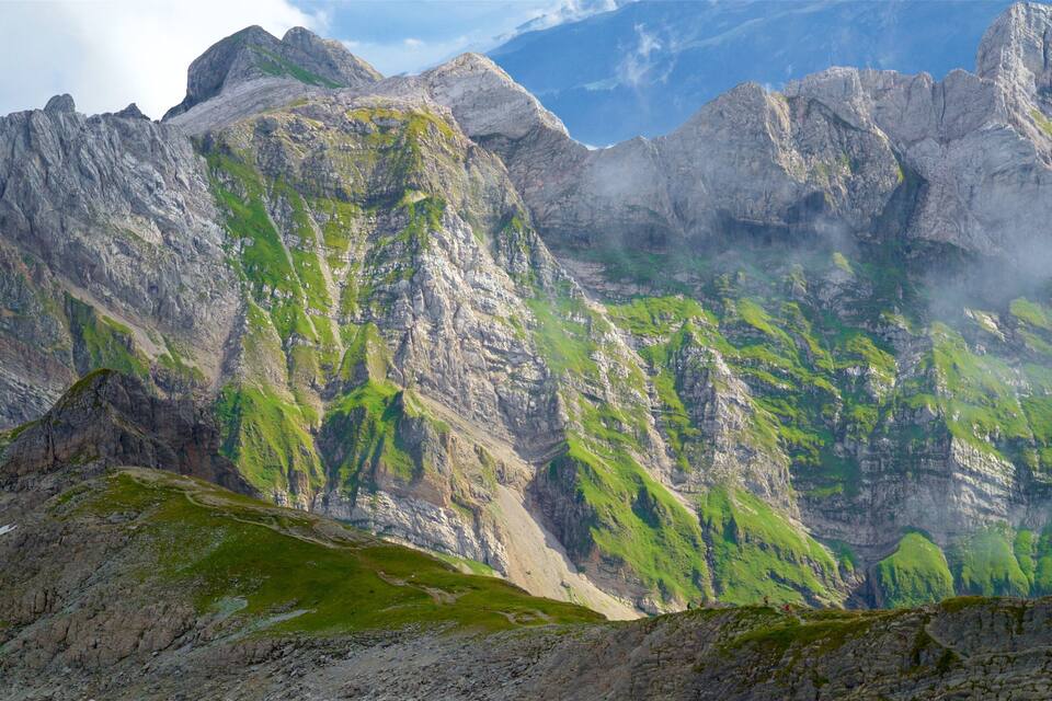 Picos montanhosos e acidentados com vegetação verde e céu limpo.