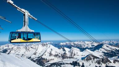 Teleférico com vista panorâmica de montanhas cobertas de neve e céu azul.