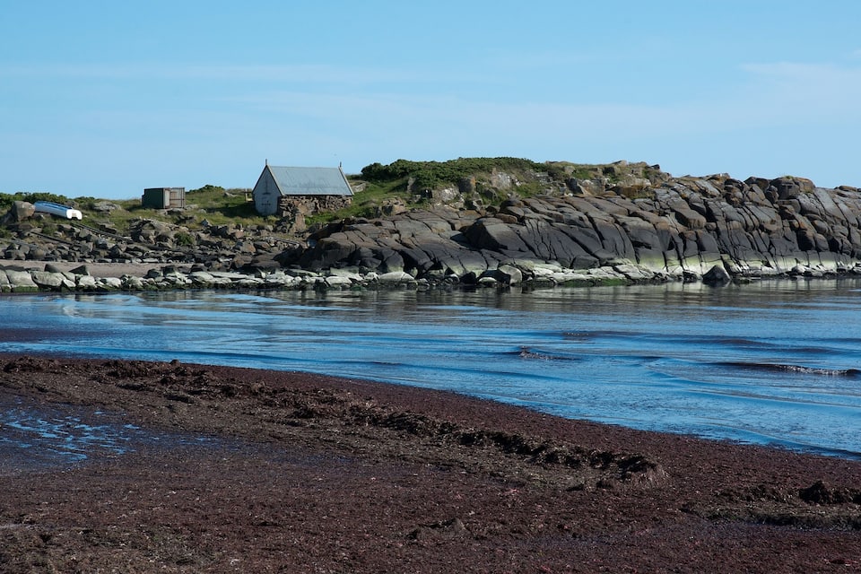 Costa rochosa com uma casa pequena e um barco.