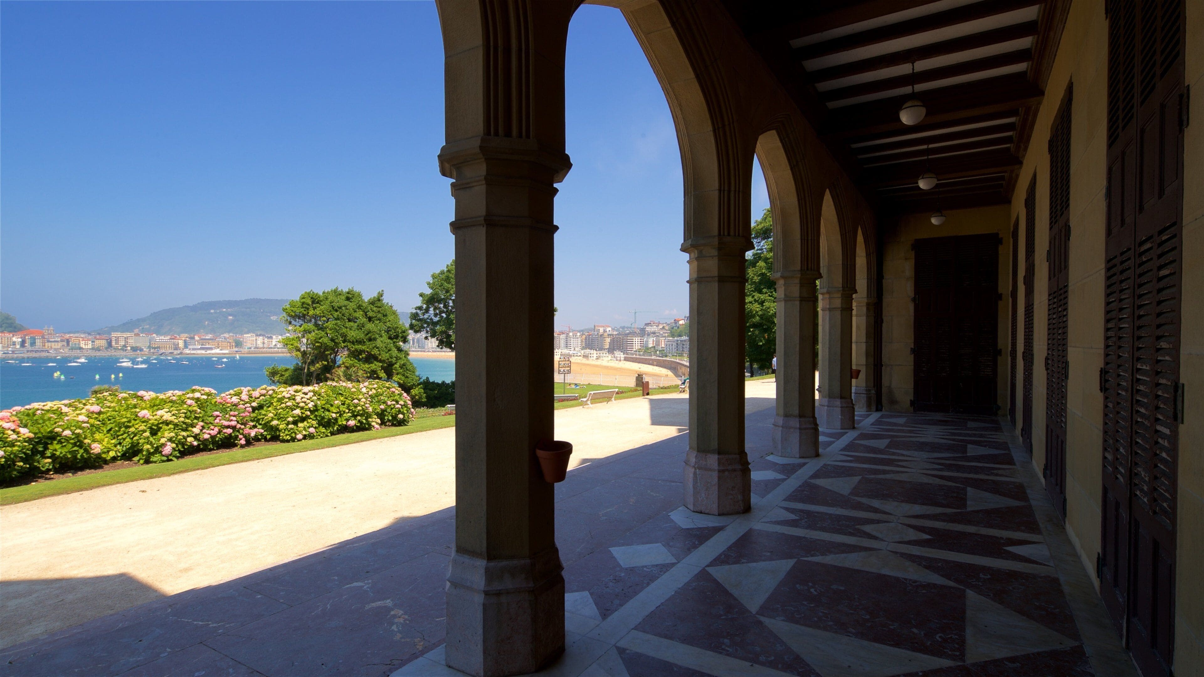 Uma galeria coberta com colunas, que leva a uma vista panorâmica do mar e da cidade.