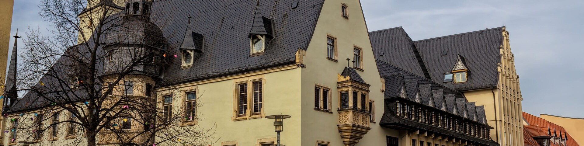Um edifício histórico com torre do relógio, rua de calçamento e pessoas caminhando.