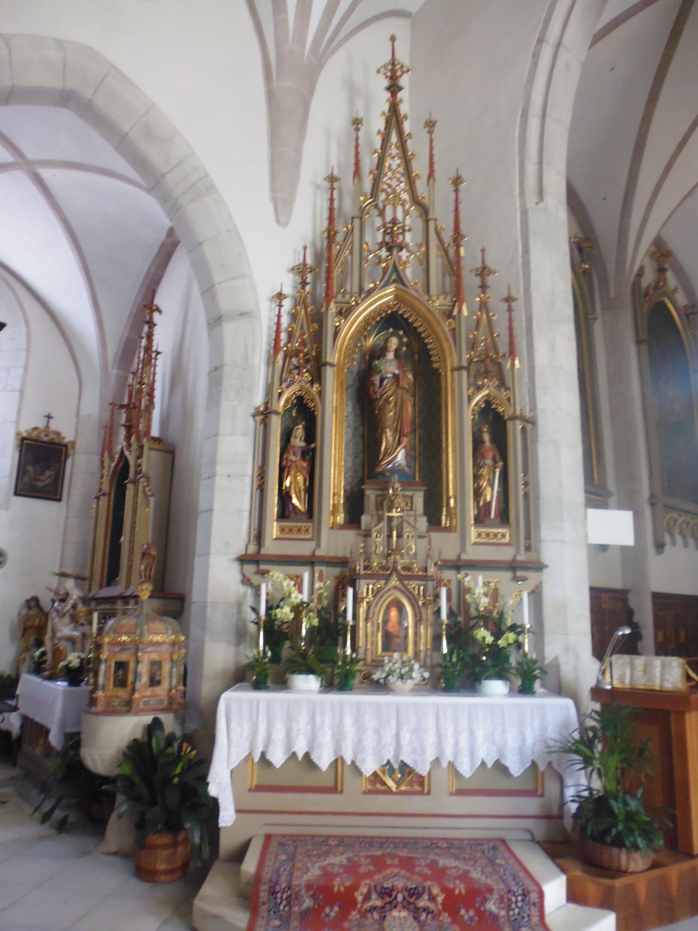 Um altar de igreja ornamentado com estátuas religiosas e uma grande cruz.