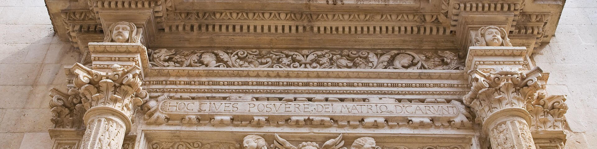 Uma entrada arquitetônica ornamentada com esculturas detalhadas e uma estátua sobre a porta.