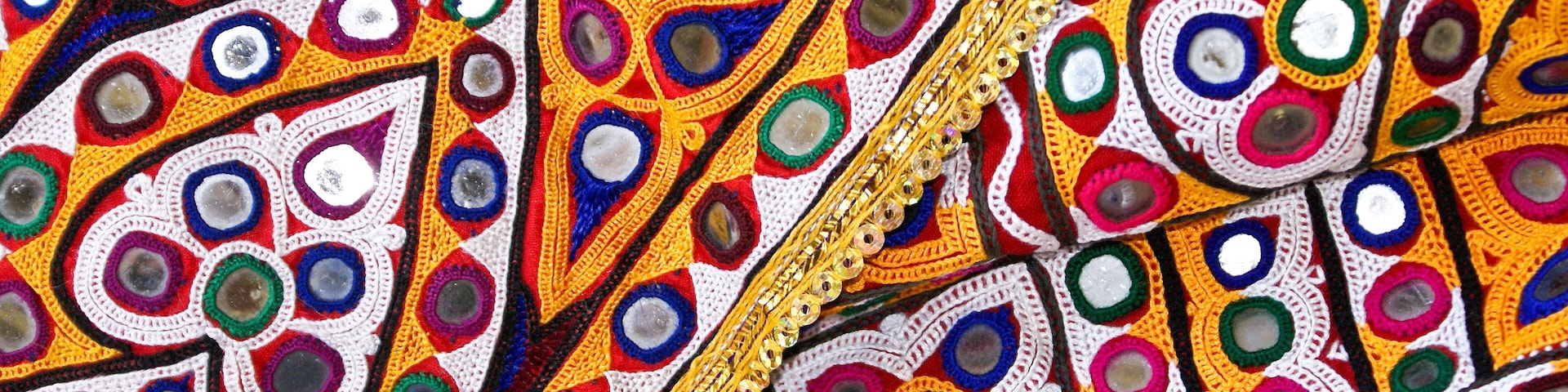Um close-up de um tecido colorido com padrões complexos, incluindo desenhos paisley e motivos circulares.