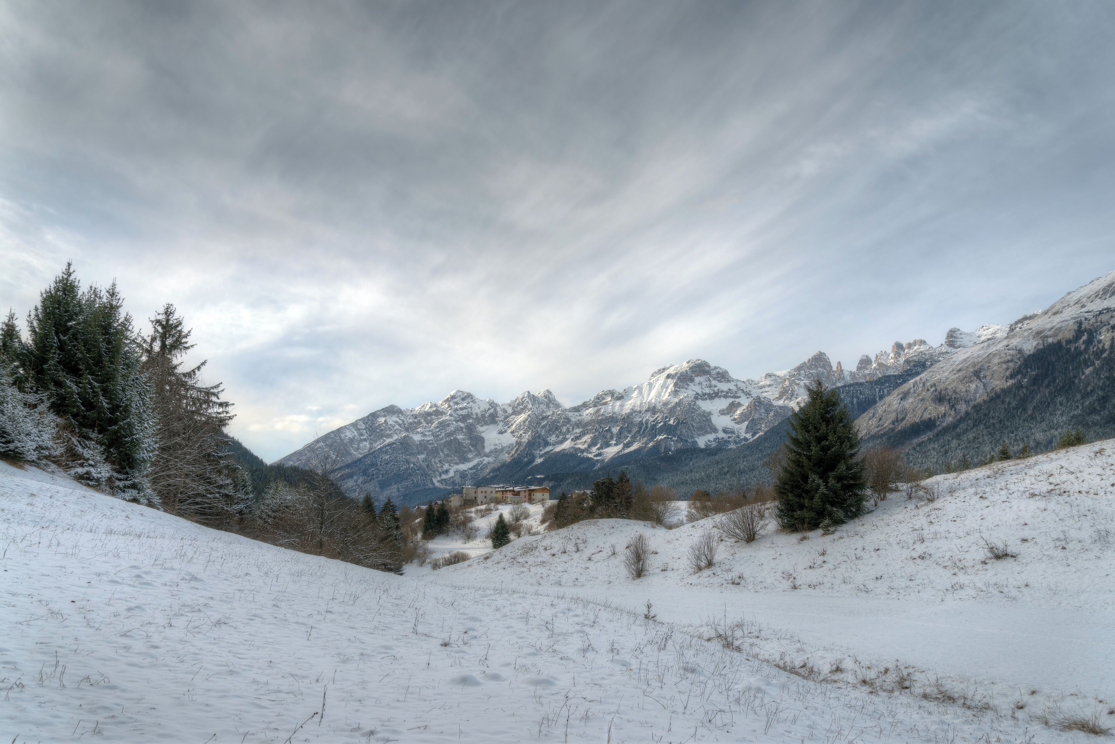 Paisagem montanhosa coberta de neve com um edifício aninhado entre árvores.