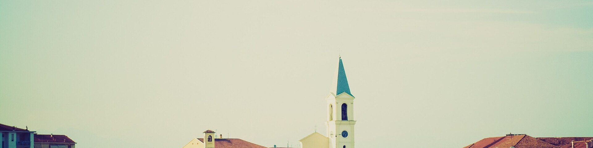 Uma cidade com telhados avermelhados, uma igreja imponente com uma torre alta e edifícios residenciais ao redor.