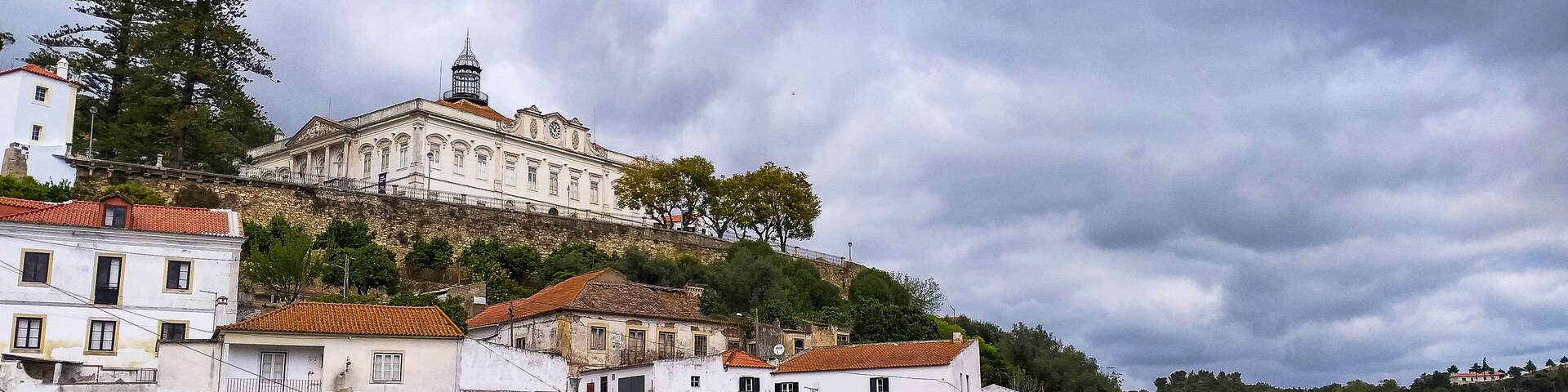 Um edifício histórico numa colina, com casas de telhados em terracota abaixo.