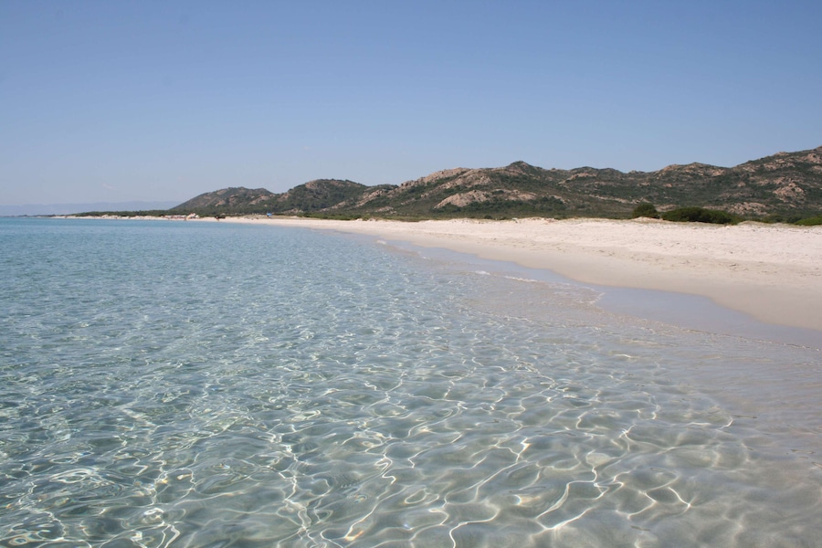 Uma praia tranquila com águas rasas e uma montanha ao fundo.