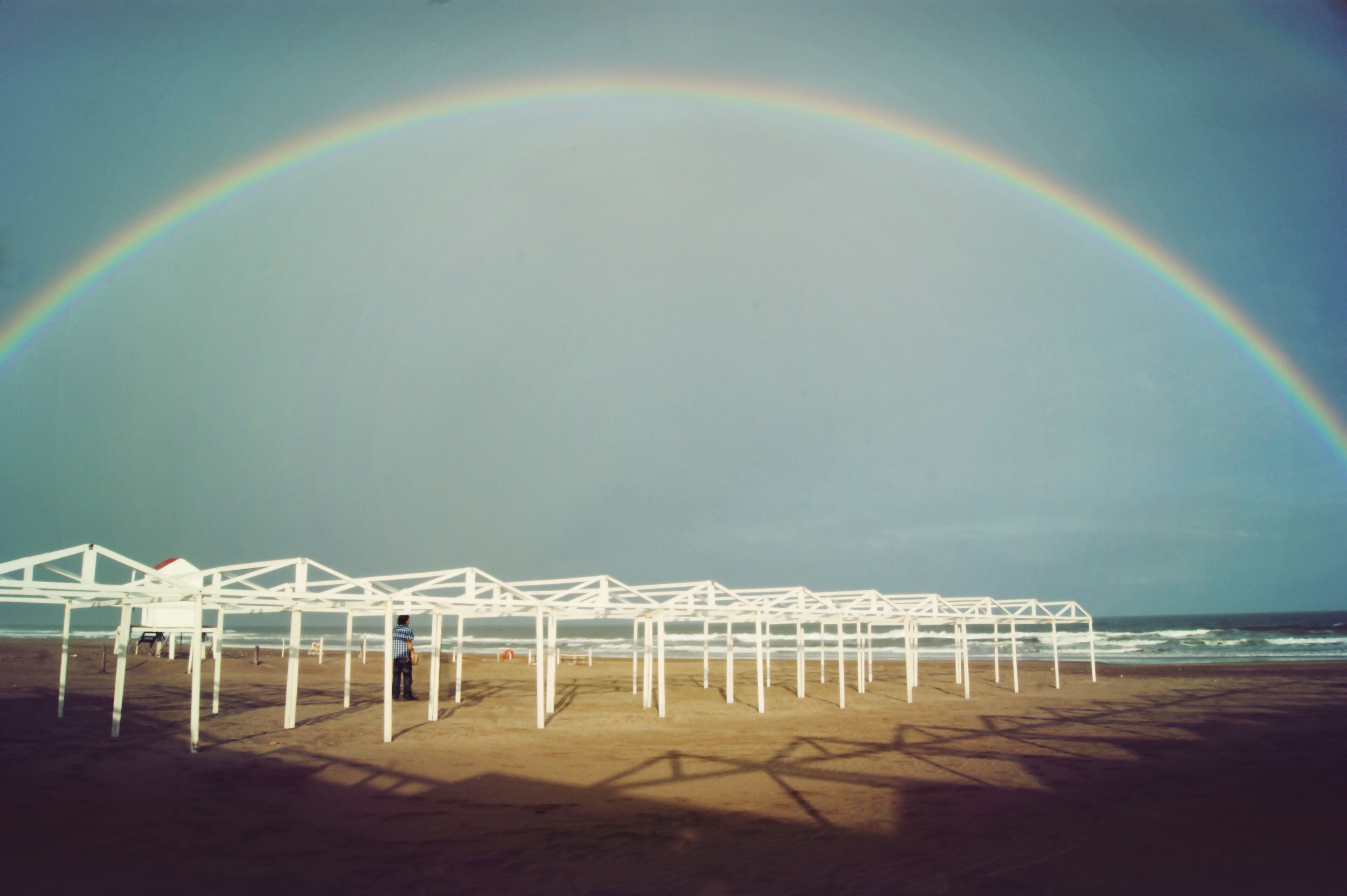 Uma praia com estruturas brancas e um arco-íris no céu.