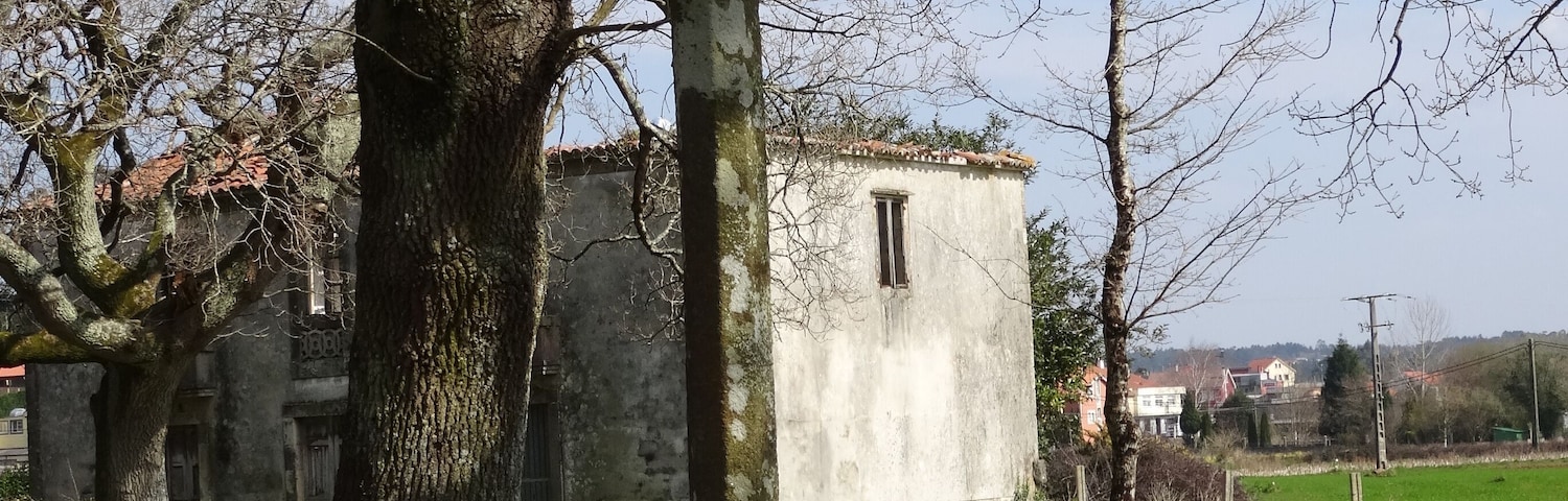 Uma cruz de pedra numa área gramada, com árvores e um edifício ao fundo.
